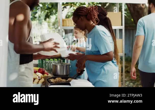 Young African American and Caucasian volunteers handing out free food ...