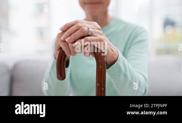 Hands, walking stick and elderly woman on a sofa with a cane for balance, support and mobility ...
