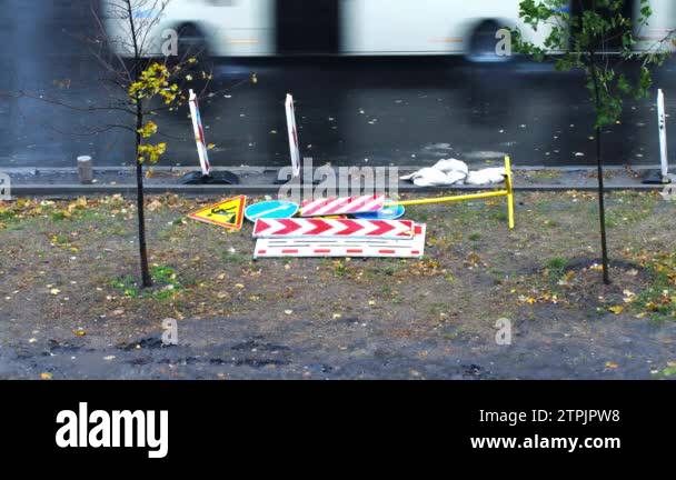 Road signs lie by the road in the rain. People with umbrellas pass and ...