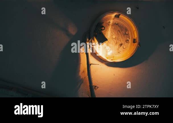 An incandescent light bulb glows in an old broken lamp on the concrete ...