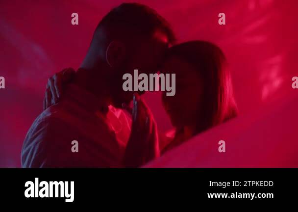 Two lovers kissing on neon light background. Woman touching face her boyfriend when kisses ...