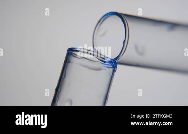 Clear fluid is poured from one tube into another in a scientific ...