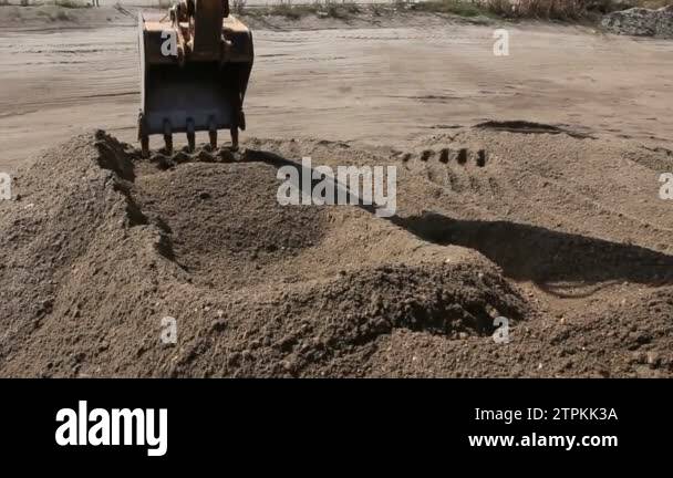 Excavator is preparing pile of sand for loading in truck on building ...