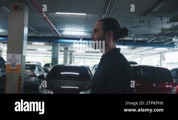 Millennial walks intently toward exit of city after parking his car ...