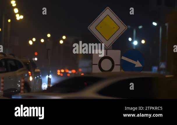 Roundabout road signs with blurred cars on city street traffic at night ...