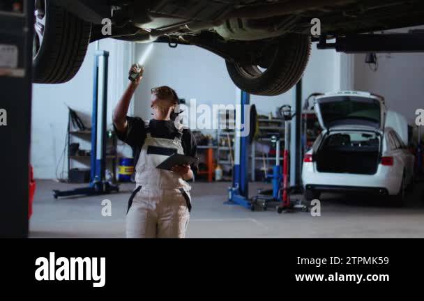 Meticulous technician underneath suspended car in repair shop, using ...