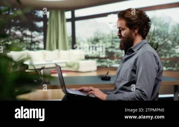 Rich adult seated at desk in his expensive lodge with massive windows ...