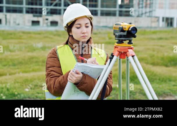 young woman surveyor in green work clothes and helmet adjusts the ...