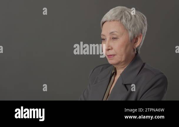 Chest up of serious mature Asian woman looking at computer monitor and ...