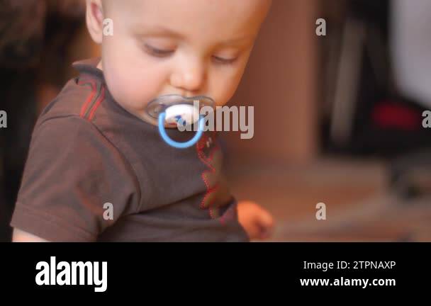 Baby boy with a soother in mouth sitting on the floor and curiously ...