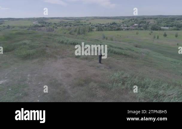 Camera circling around a man standing on the top of a hill and lifting ...