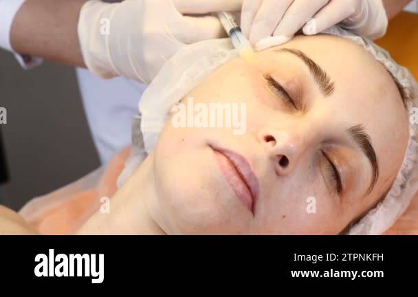 Cosmetician in gloves making face lifting injection to area around eyes ...