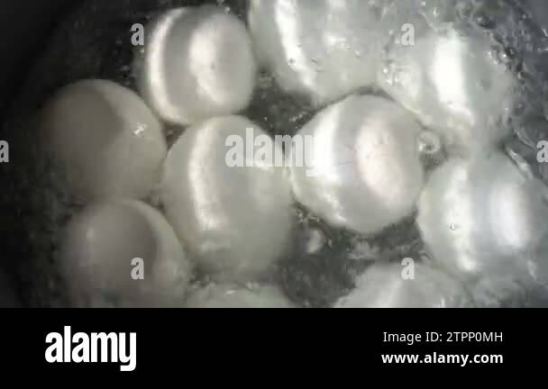 White eggs are boiled in boiling water in a metal pan. One egg cracked ...