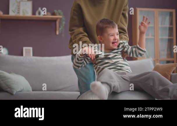 Laughing Caucasian 6 year old boy with down syndrome having fun while jumping on fitness ball ...