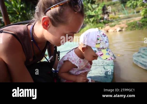 Mother and her daughter are feeding the koi fish in pond by milk bottle ...