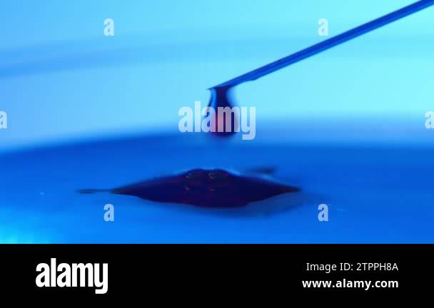 Small drops of blood fall from a metallic needle on a blue glass ...
