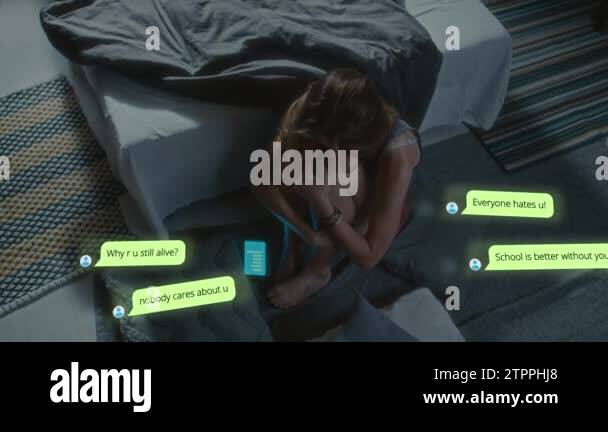 Top down shot of young girl sitting on floor in dark bedroom, reading threatening messages on ...