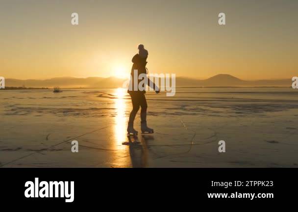 LENS FLARE, SILHOUETTE: Early winter morning with lady skating on a ...