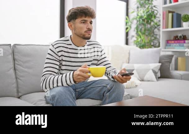 Chilled-out young arab man smiling as he enjoys his morning espresso, comfortably relaxed ...