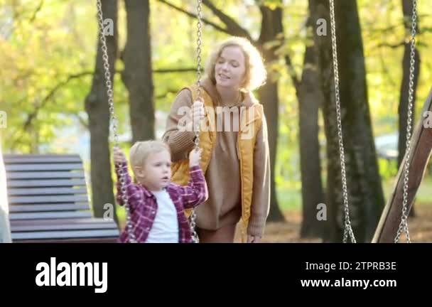 A mother swings her son on a swing in an autumn city park. A beautiful ...