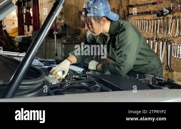 Young woman in coveralls works at a car service station conducting ...