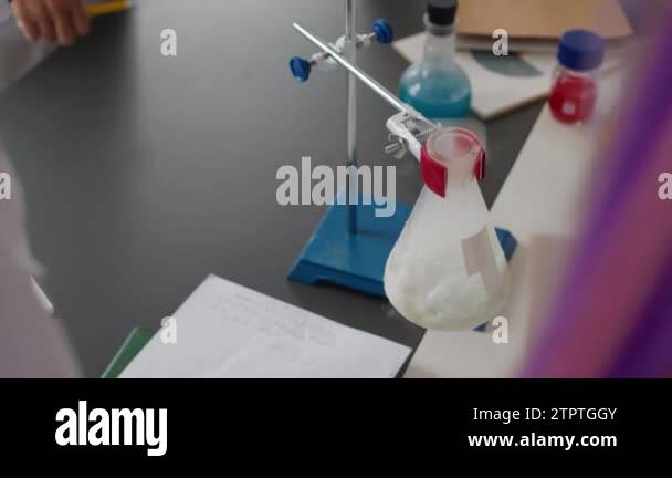 Cropped shot of unrecognizable student in lab coat pouring ...