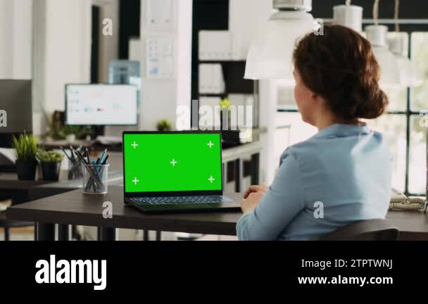 Team leader analyzes greenscreen display on laptop, working on business operations in open floor ...