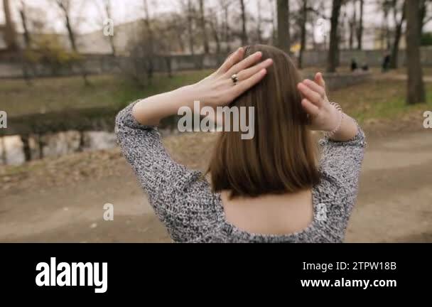 Woman tying her smooth hair in ponytail, making hairdo, back view ...