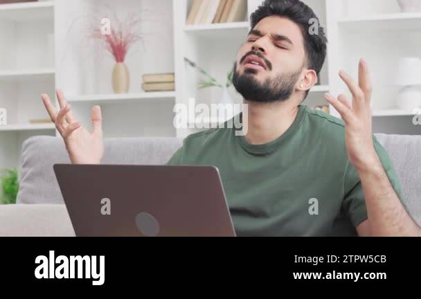 Bearded male freelancer asking for good luck with crossed fingers while looking at laptop screen ...