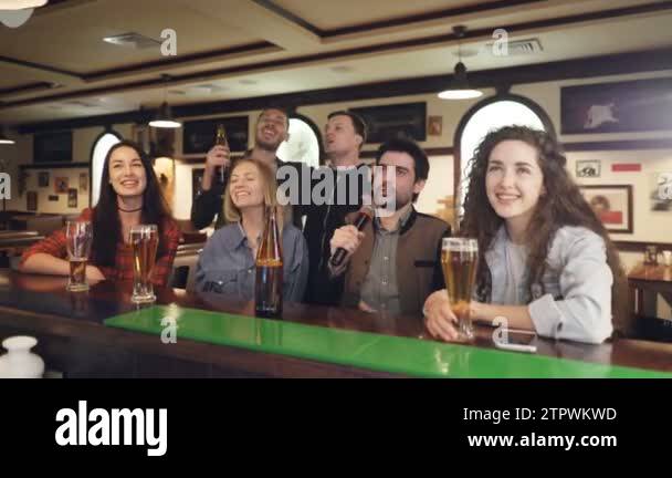 Happy young friends are singing karaoke while drinking beer in modern ...