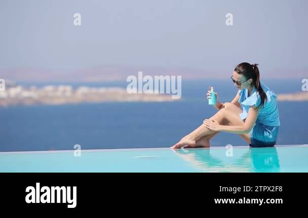 Slim Woman Applying Sunscreen On Her Legs Sitting On The Edge Of Pool
