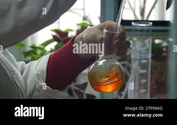 Male hand rotates a glass flask with yellow liquid and a tube in a ...