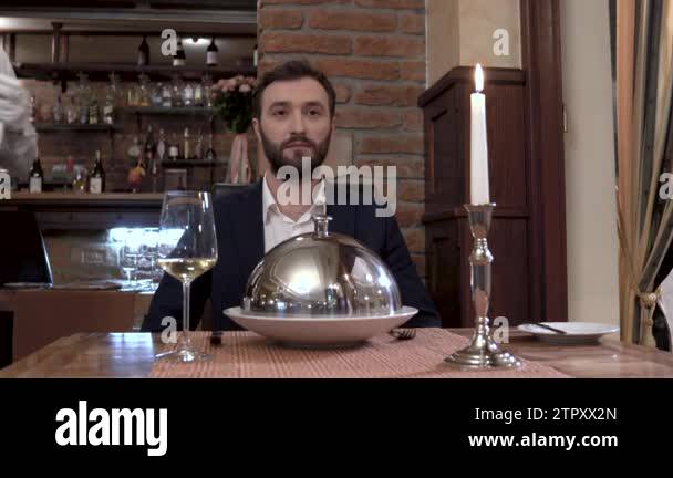 Waiter corrects placement of the glass and opens cloche showing the ...