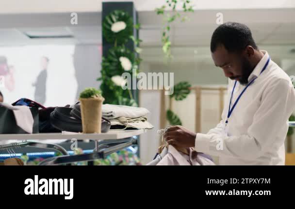 Elegant worker arranging clothes in mall clothing store with fast ...