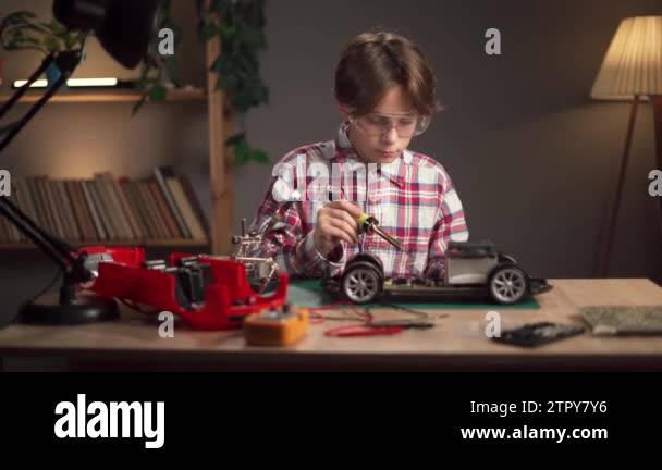 Pretty concentrated boy repairing a broken toy car in his room, child soldering wires and parts ...