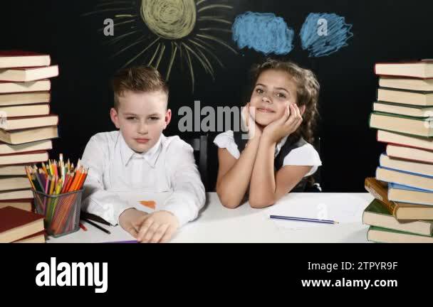 Back to School concept. Boy and girl sit at a desk with heaps of books ...