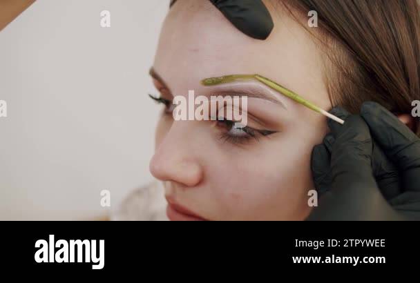 Beautician applying epilation wax to eyebrows of young woman client for ...