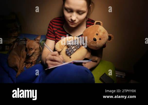 Teenage writing diary at home in her bad with a toy bear and little ...