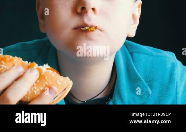 Teen alternately eating a hamburger and greasy fried chicken wings in ...