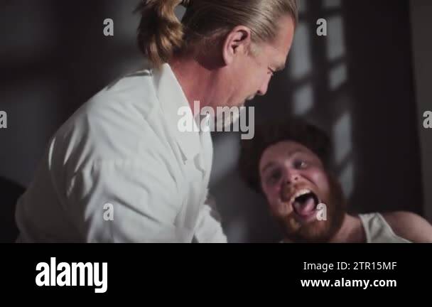 Insane patient screaming and resisting while mature doctor tying him to ...