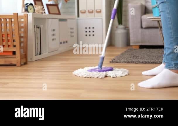 Woman uses mop to wipe the floor back and forth in the living room at ...