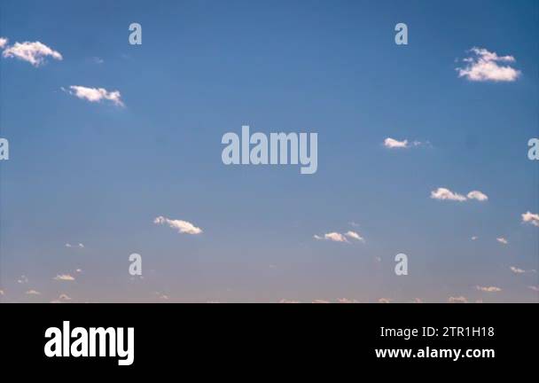 White fluffy clouds slowly float through the blue daytime sky timelapse ...