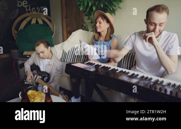 Musical band is practising at home, guitarist is sitting on floor and ...