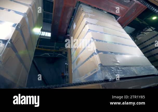 Wrapping material is getting tightened around a stack of carton boxes with glass bottles. 4K ...