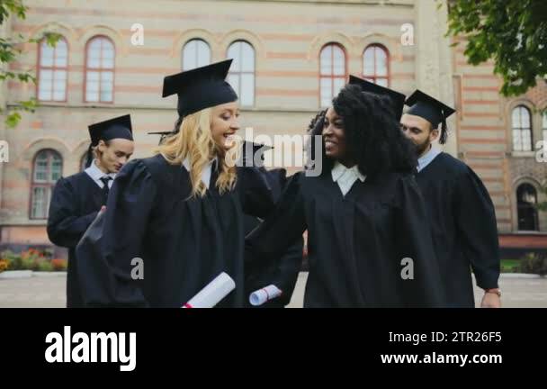 Happy smiled mixed races graduates walking with the diplomas in hands ...