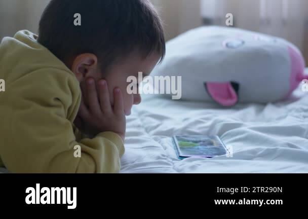 Cute preschool child lying on the bed and watching cartoons on the ...