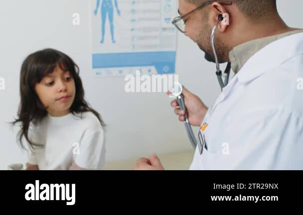 Waist up of Middle Eastern male doctor holding stethoscope to little ...