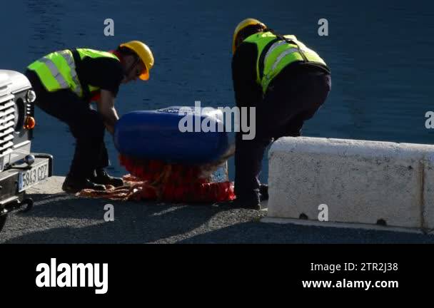 Maritime workers casting off mooring lines of a large boat at the dock ...