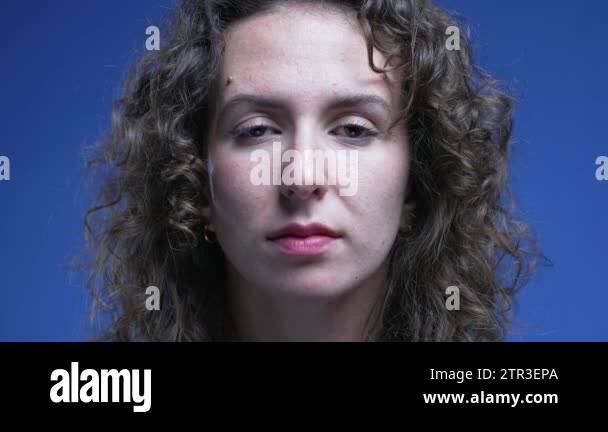 Close-up woman face looking at camera with neutral expression, blue ...