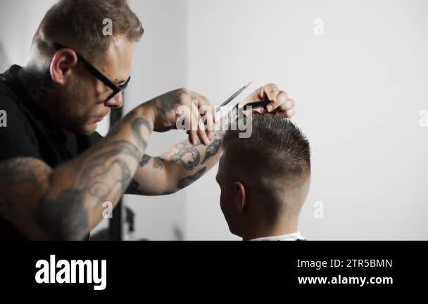 Tattoed barber makes haircut for customer at the barber shop by using ...